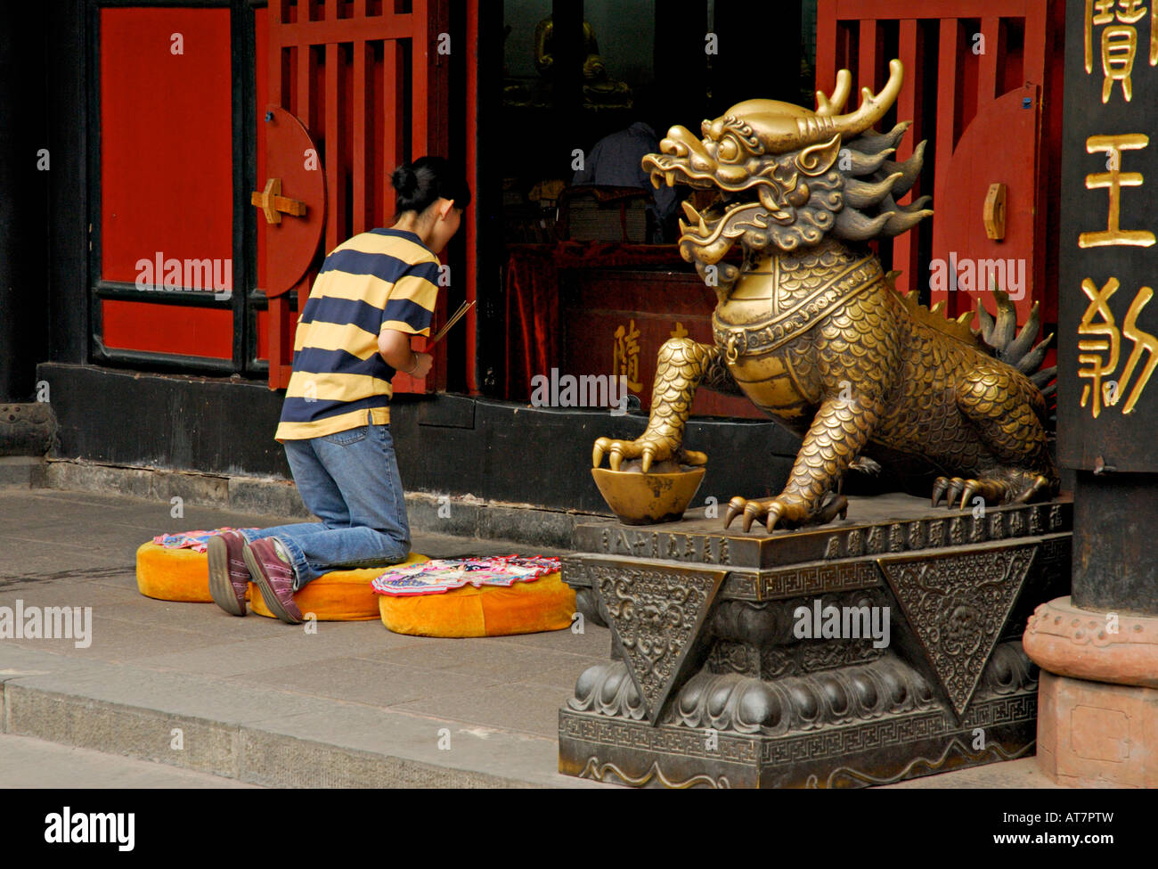 Chinese Buddhist prays at a shrine at Wenshu Temple guarded by a ...