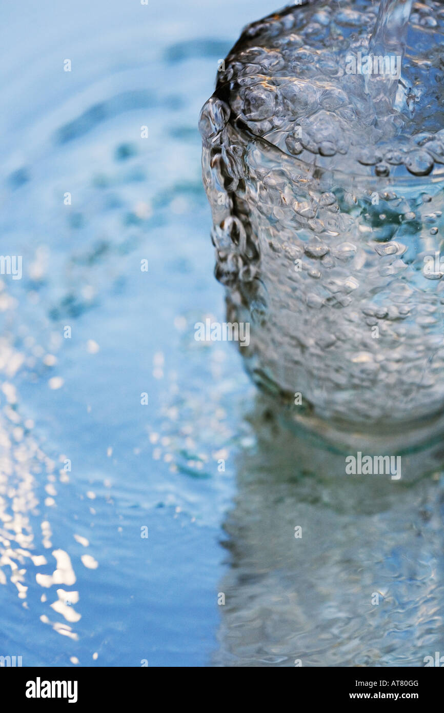 Water pouring into a glass that stands on a mirror which reflects blue ...