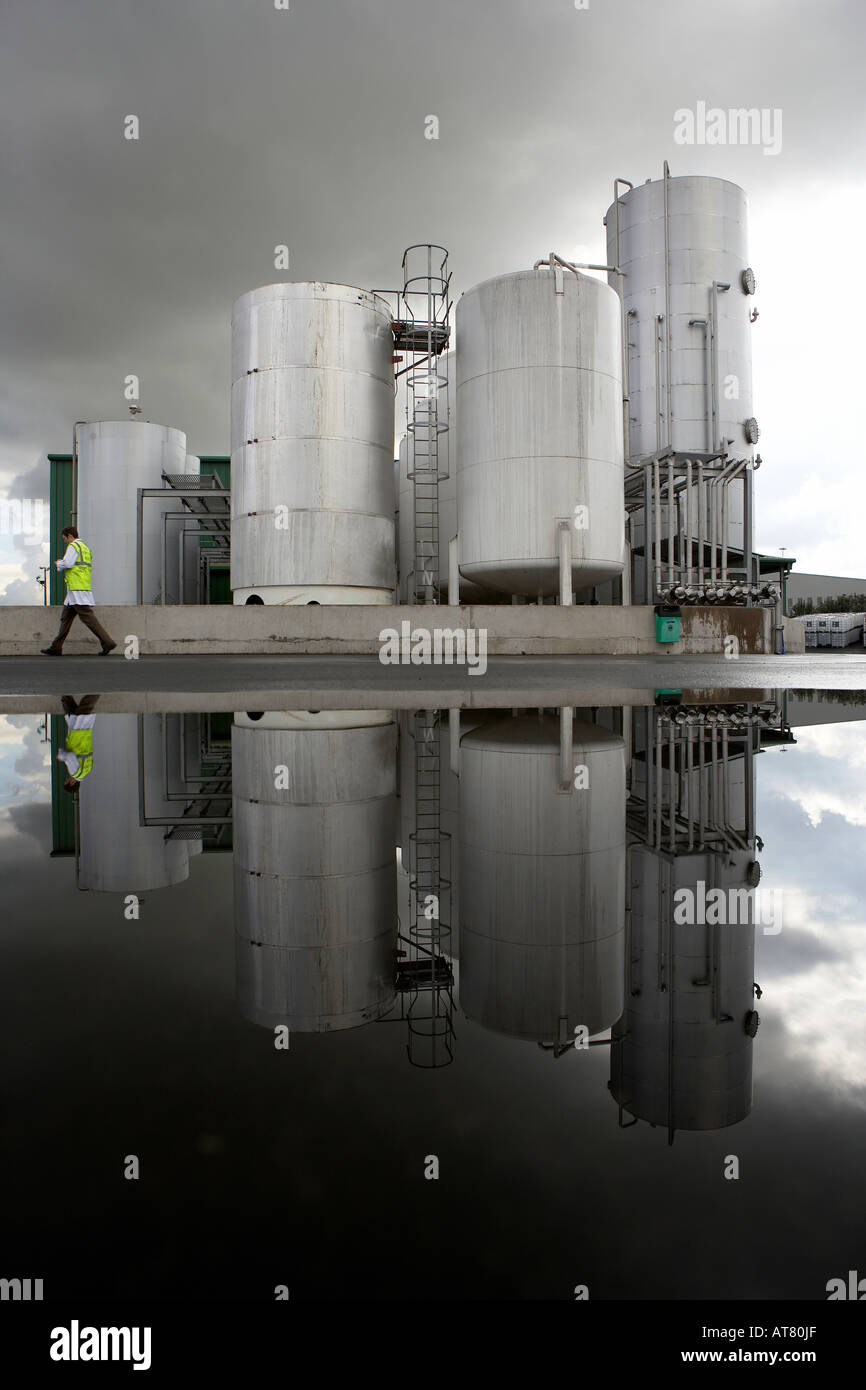 Worker and a bulk liquid storage facility reflected in a pool of water ...