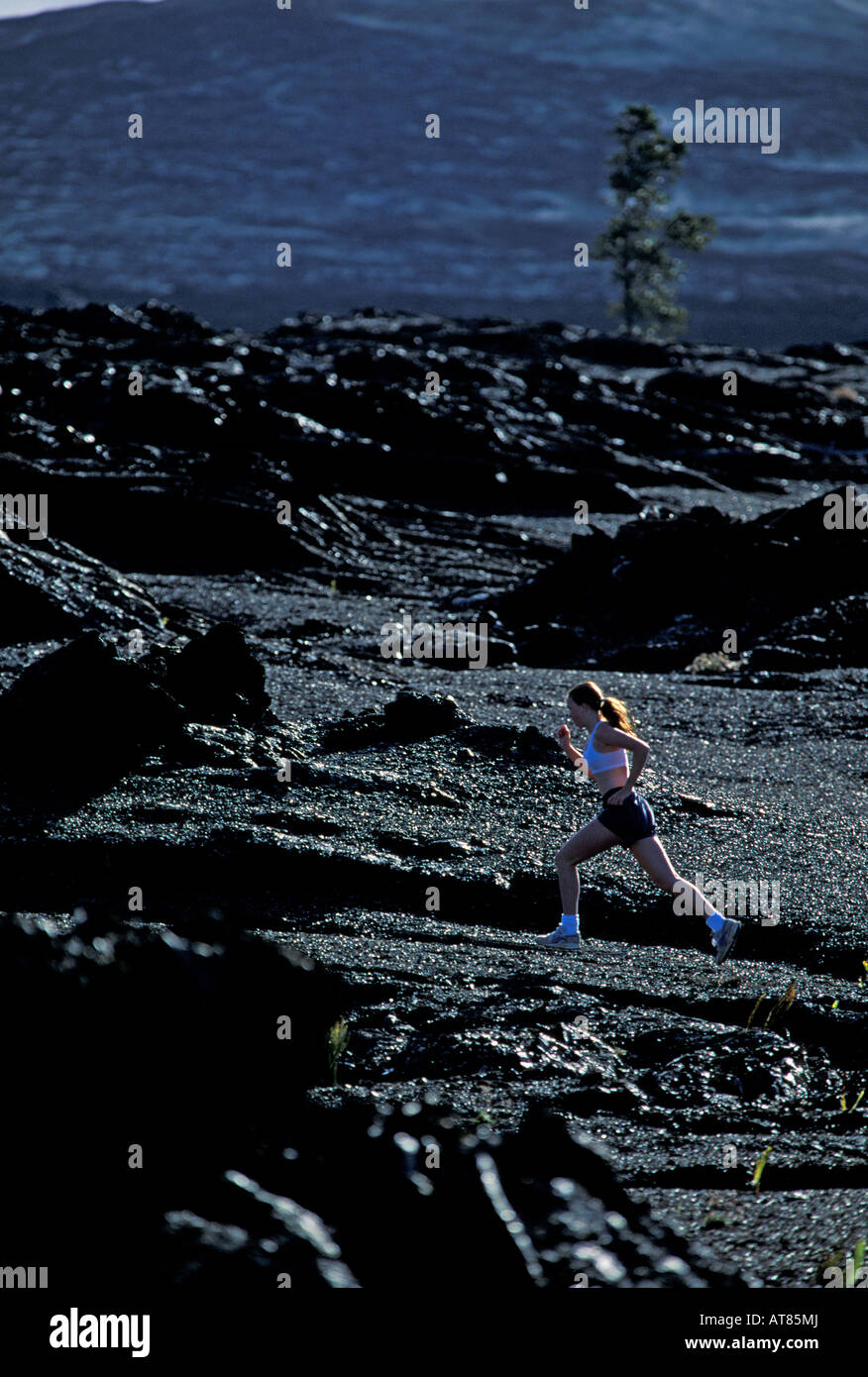 Young woman running on the black lava fields at Volcanoes National Park ...