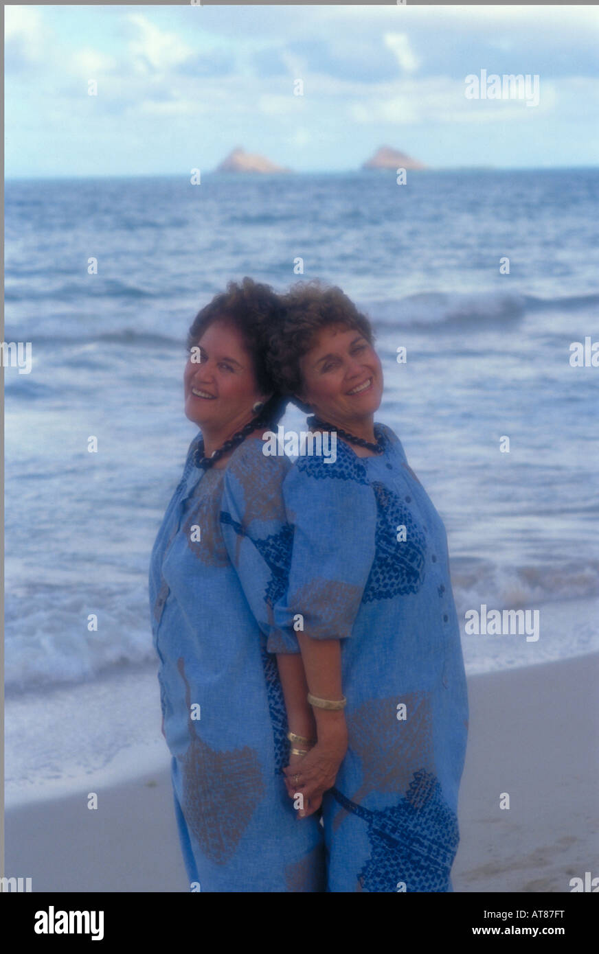 Portrait of smiling twin sisters wearing blue aloha wear at Kailua ...