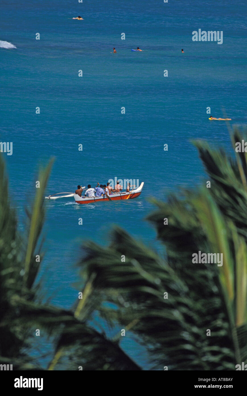 group of tanned local paddlers navigate their Hawaiian outrigger canoe ...