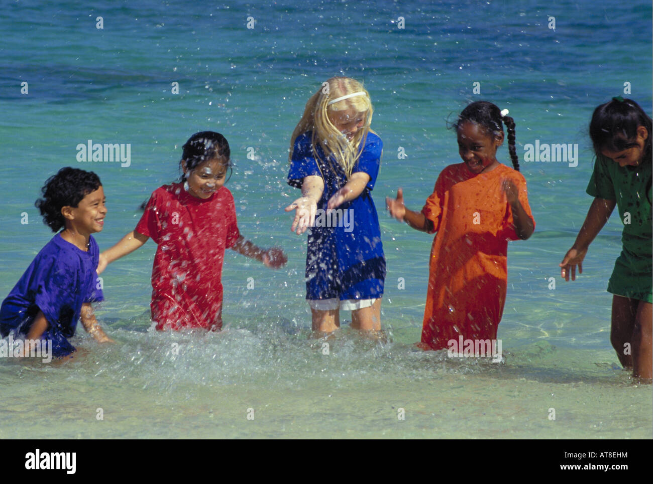 Children wearing bright colorful clothes splash water near the shore at ...