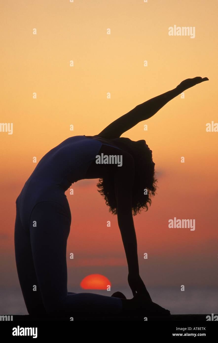 The silhouette of a woman doing a yoga back pose with an orange sun ...