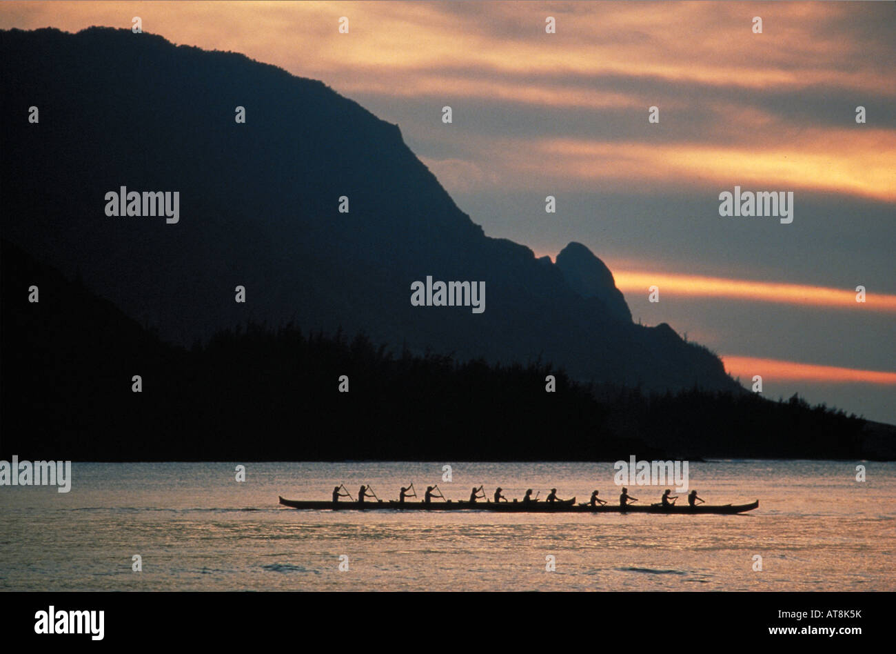 An outrigger canoe team paddles against a beautiful sunset at Makana ...