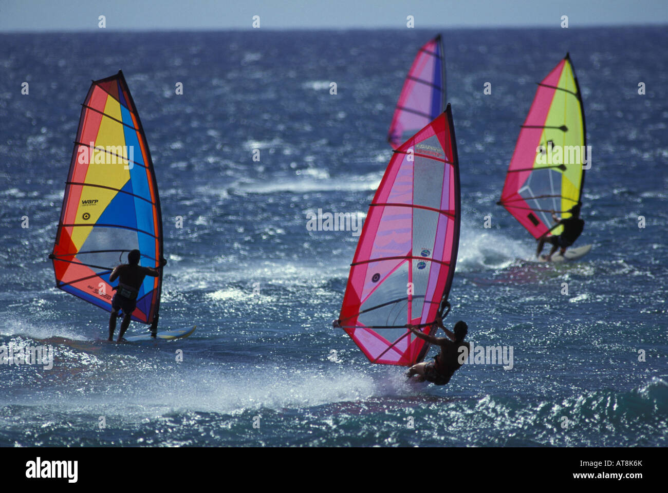 Windsurfers with their colorful sails cut through the blue ocean at ...