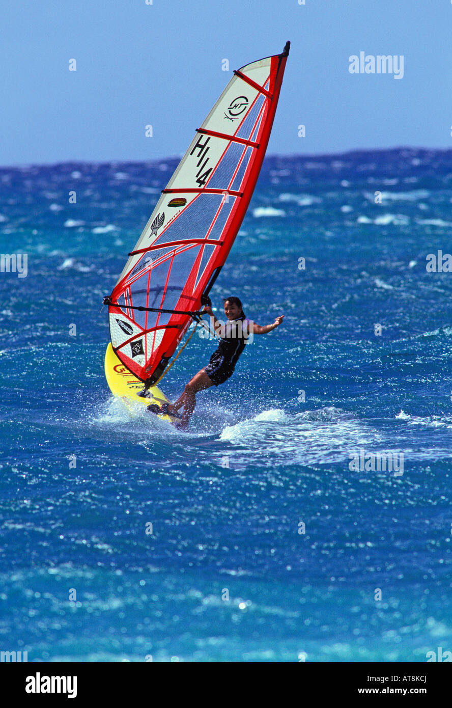 A young woman windsurfer takes a thrilling ride on the clear blue ocean ...