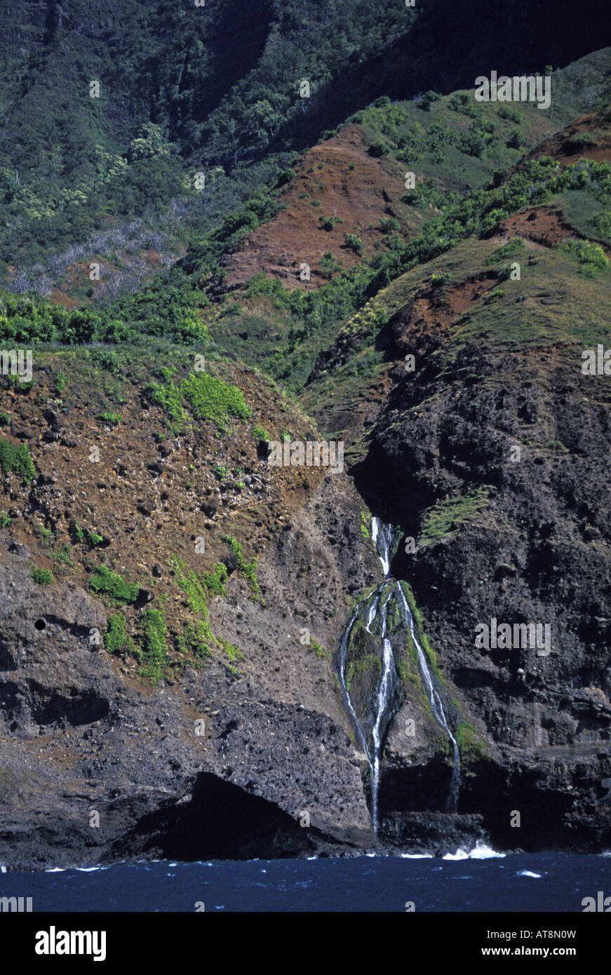 Waterfall breaking between steep rock faces drops into deep blue ...