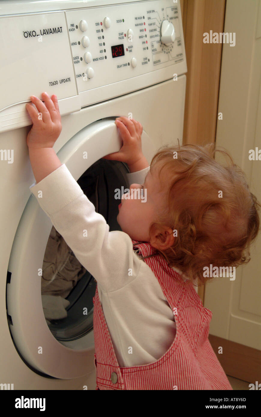 Toddler standing in the kitchen and looking at a washing machine Stock ...