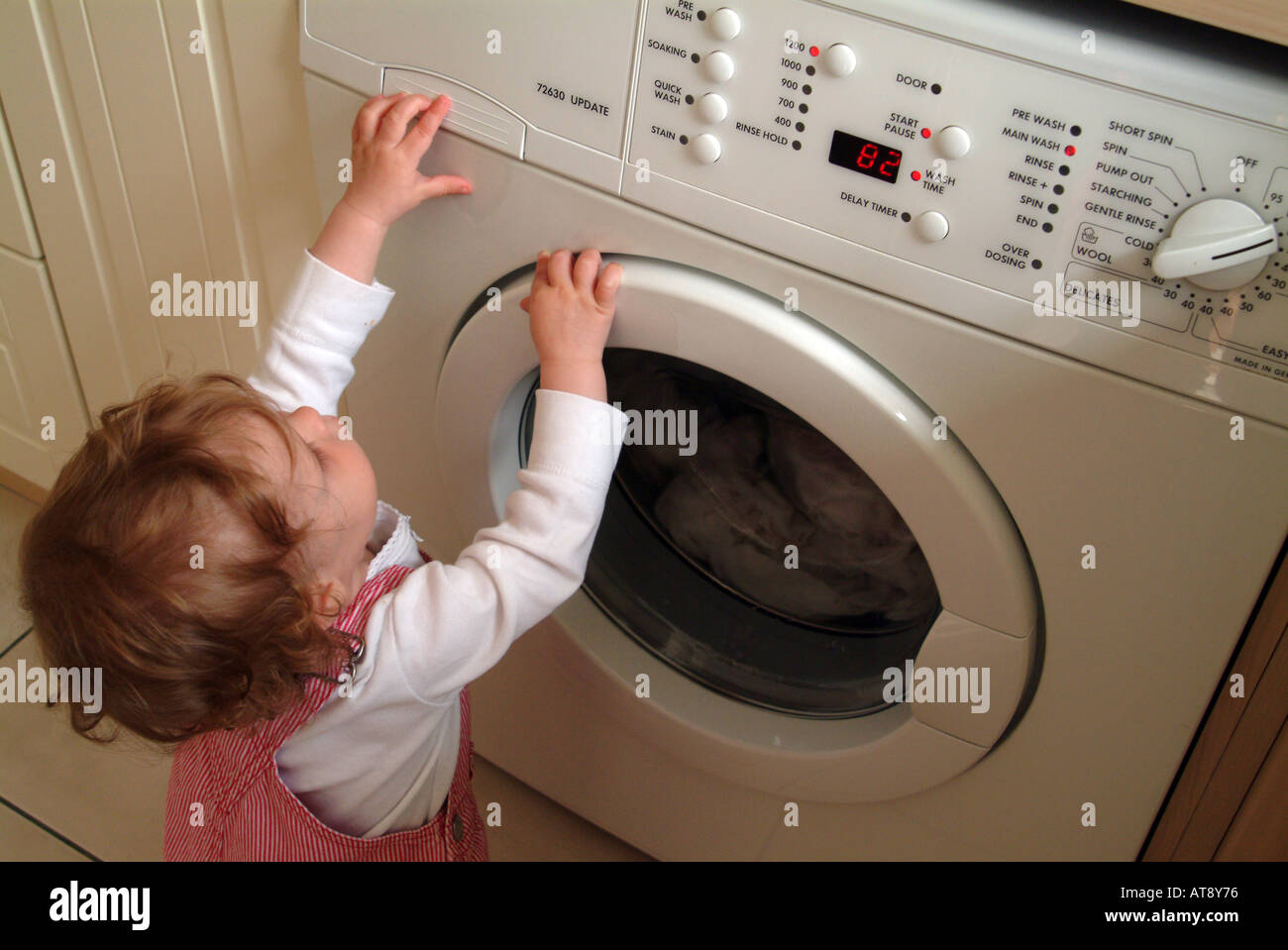 Toddler standing in the kitchen and looking at a washing machine Stock ...