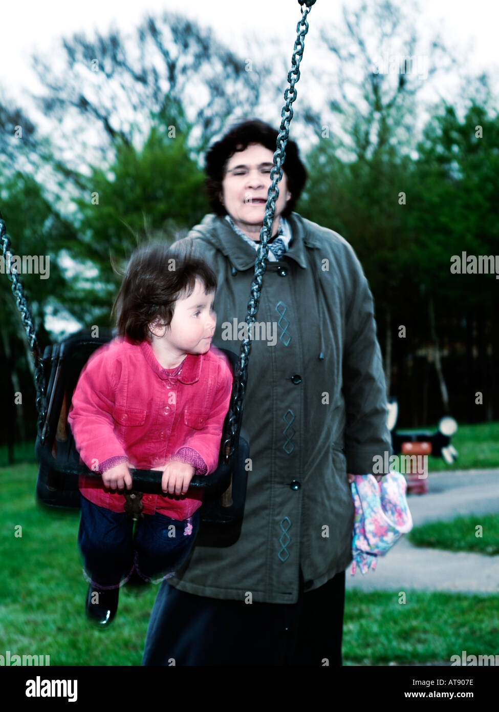 grandmother pushing a child on a swing in a play area Stock Photo - Alamy