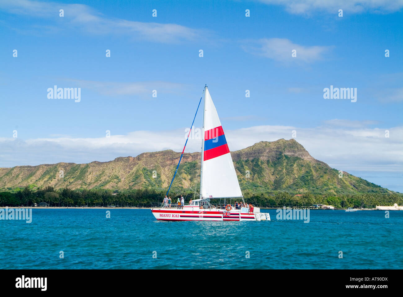 A catamaran with a red and blue striped sail glides on blue water with ...