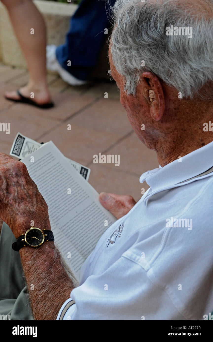 Adulty senior male wearing hearing aid reading book Stock Photo - Alamy