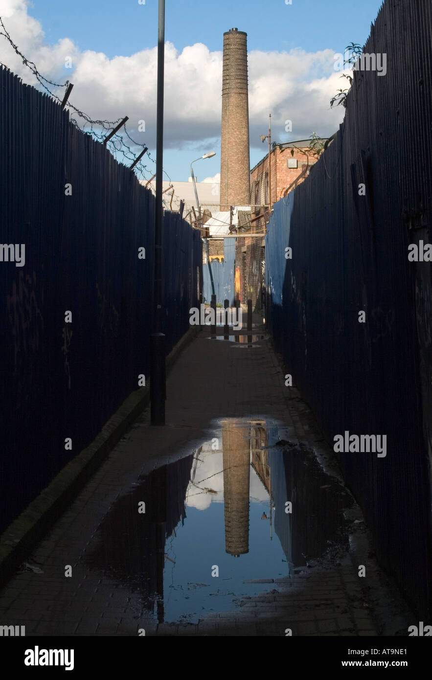 Industrial chimney seen in puddle, in narrow corrugated iron and barbed ...