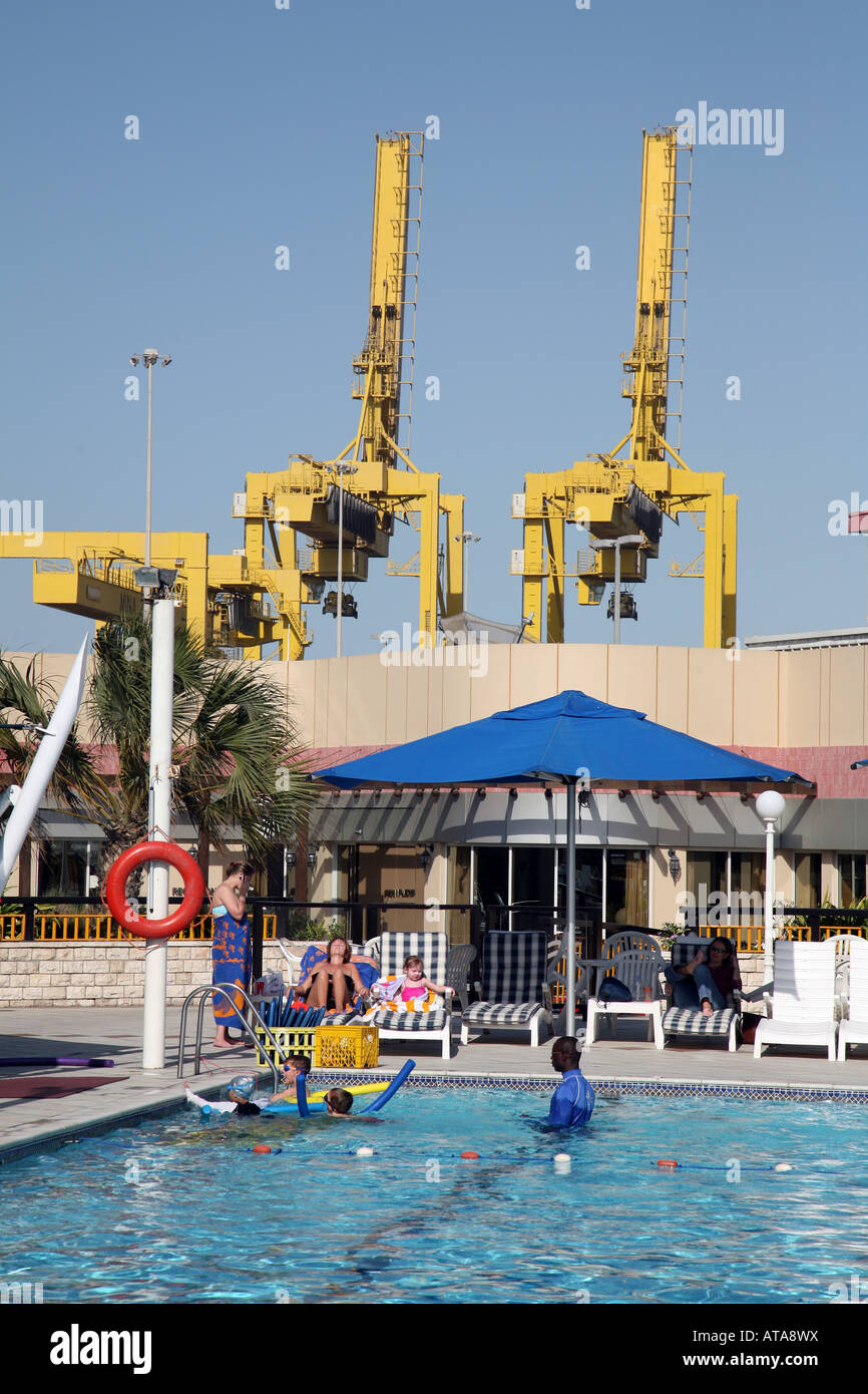 Tourists enjoy the swimming pool with large harbour cranes in the ...