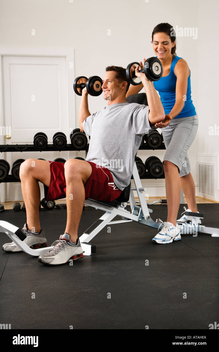 Woman assisting man lifting weights at gym Stock Photo - Alamy