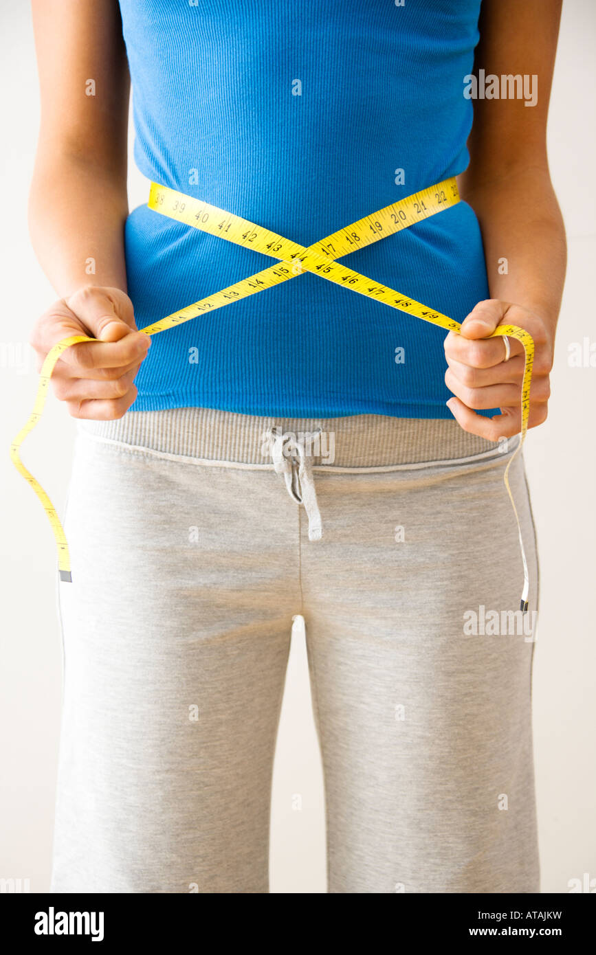Woman standing pulling measuring tape around waist Stock Photo - Alamy