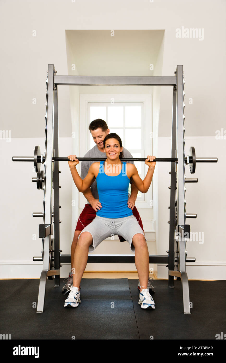 Woman lifting weights in gym being assisted by man Stock Photo - Alamy