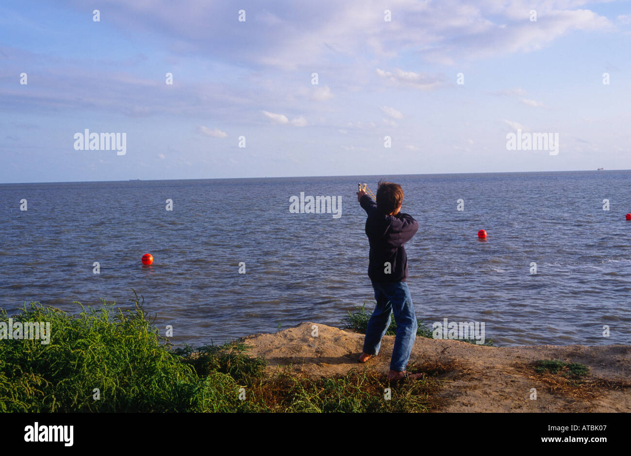 Boy firing his catapult into the sea with two red bouys Stock Photo - Alamy
