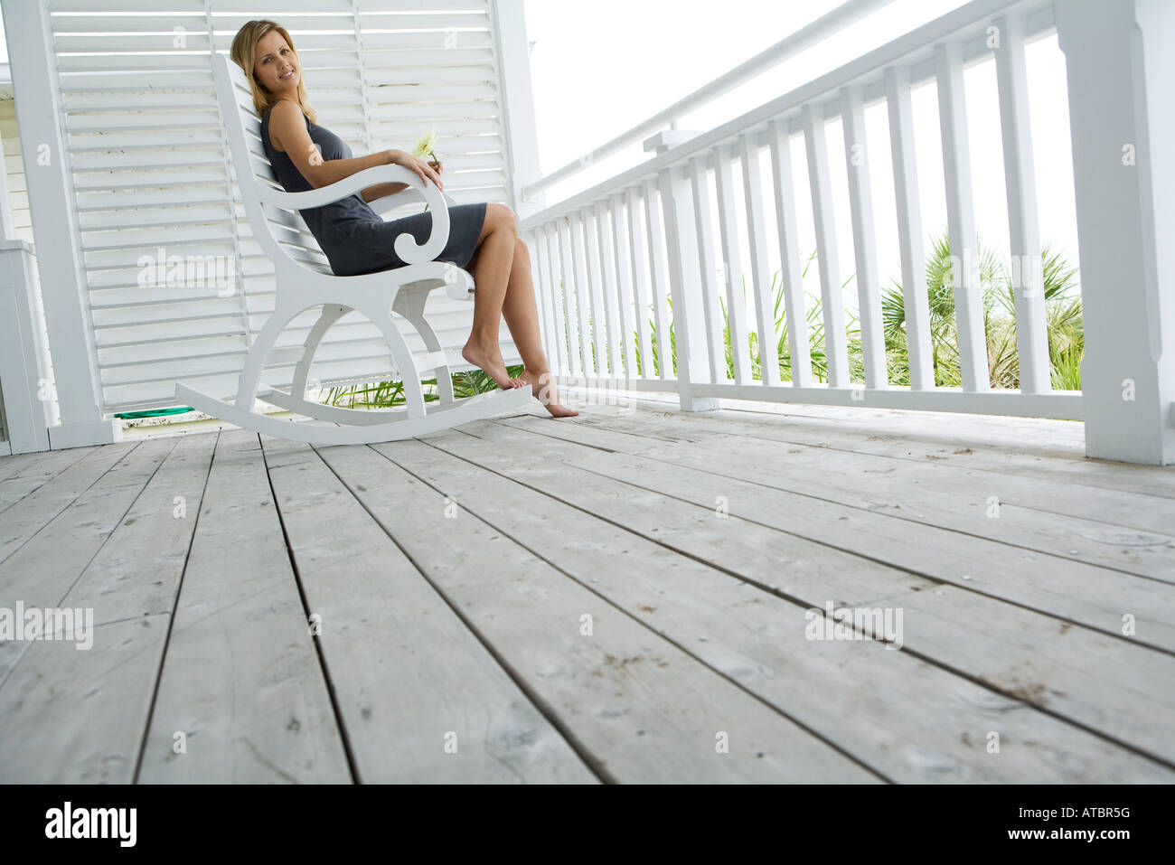 Woman sitting in rocking chair on porch, holding flower, smiling at ...