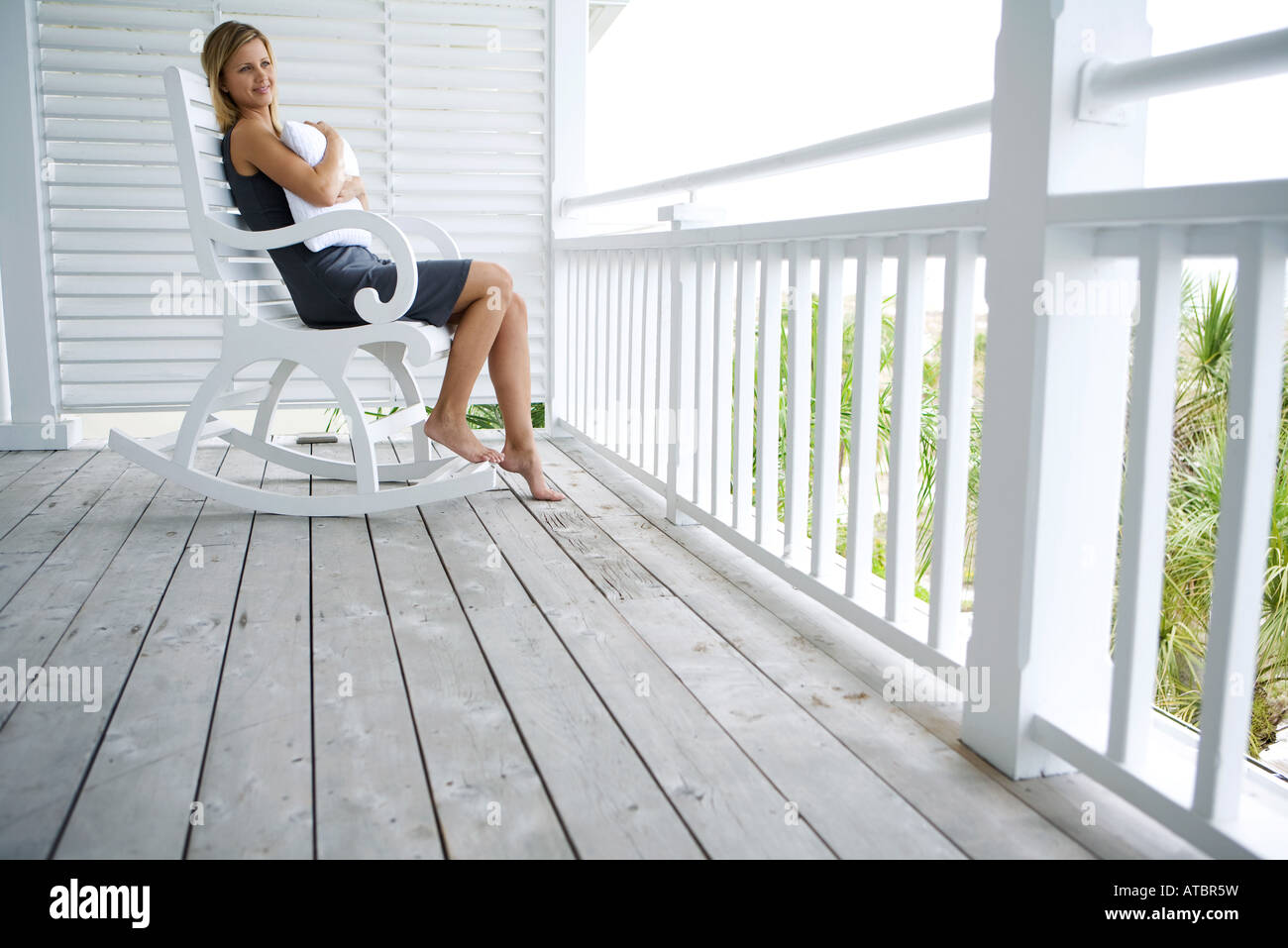 Woman sitting in rocking chair on porch, hugging pillow, looking away ...