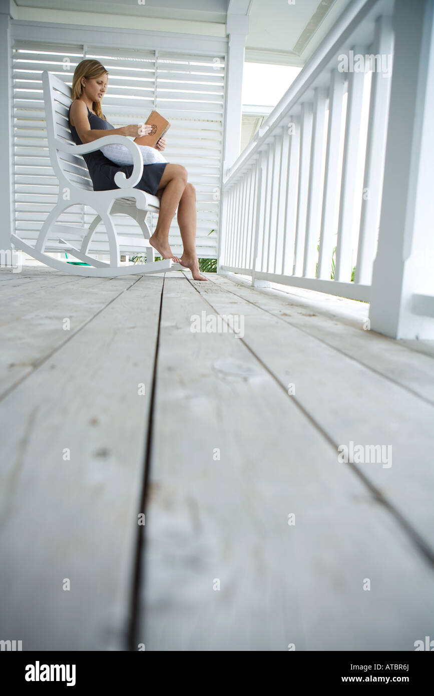 Woman sitting in rocking chair on porch, reading book, low angle view ...