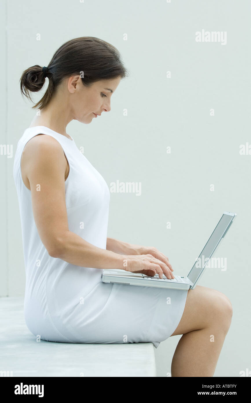 Woman sitting, using laptop computer, side view Stock Photo - Alamy