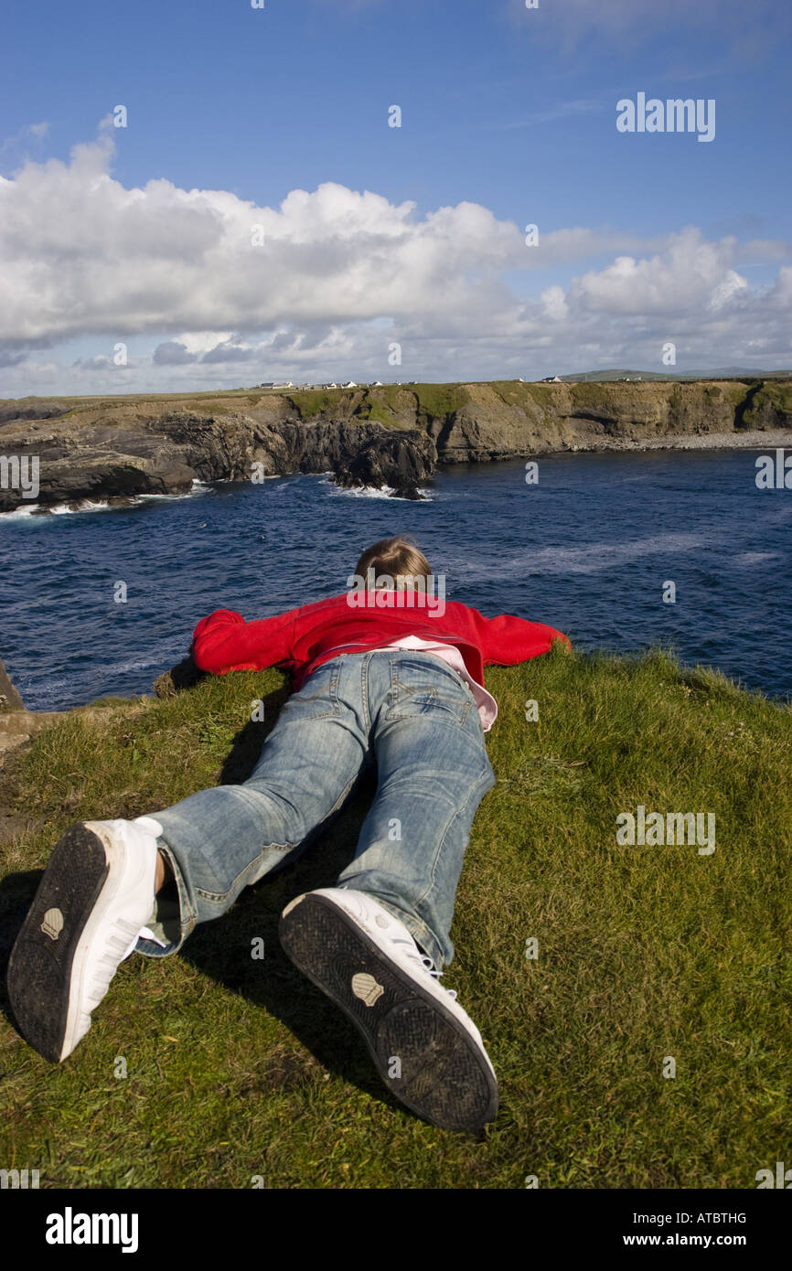boy lying on the ground and looking over a cliff edge; western coast of ...