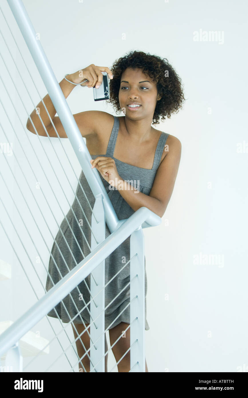 Young woman leaning against railing, holding up digital camera Stock ...