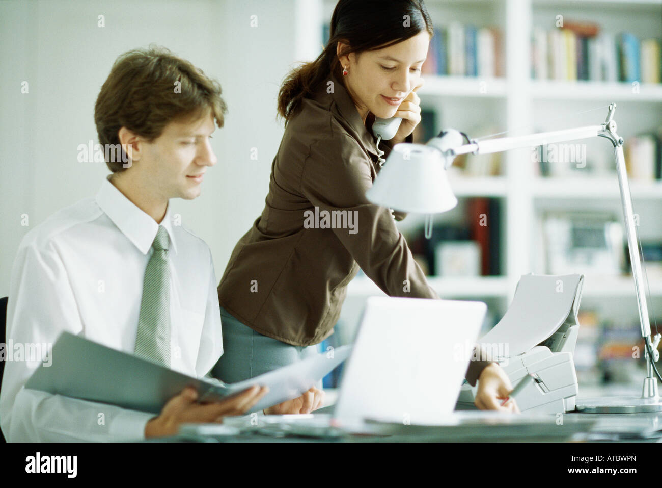 Male and female colleagues at desk, man looking at laptop computer ...