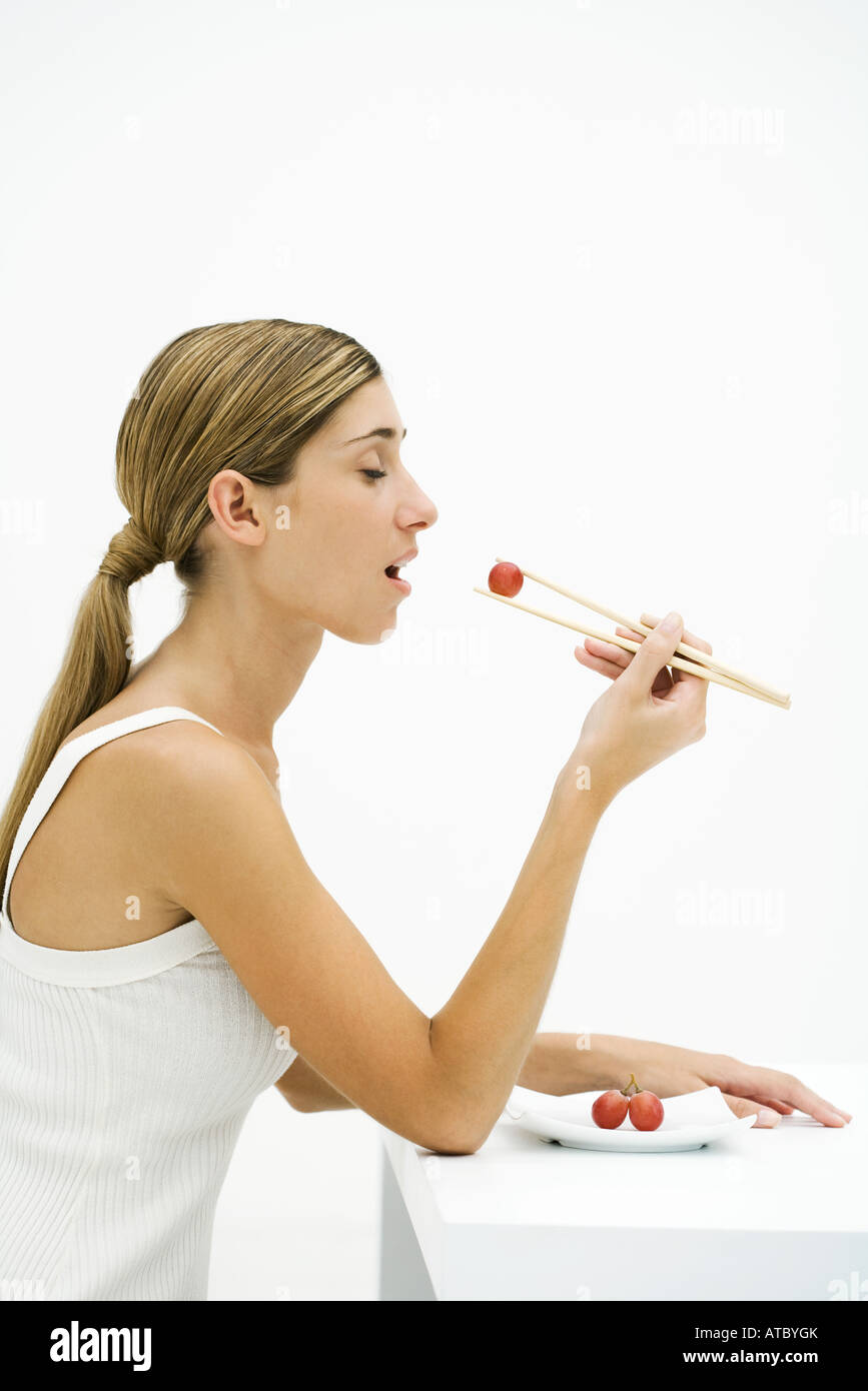 Woman eating red grape with chopsticks, eyes closed, side view Stock ...