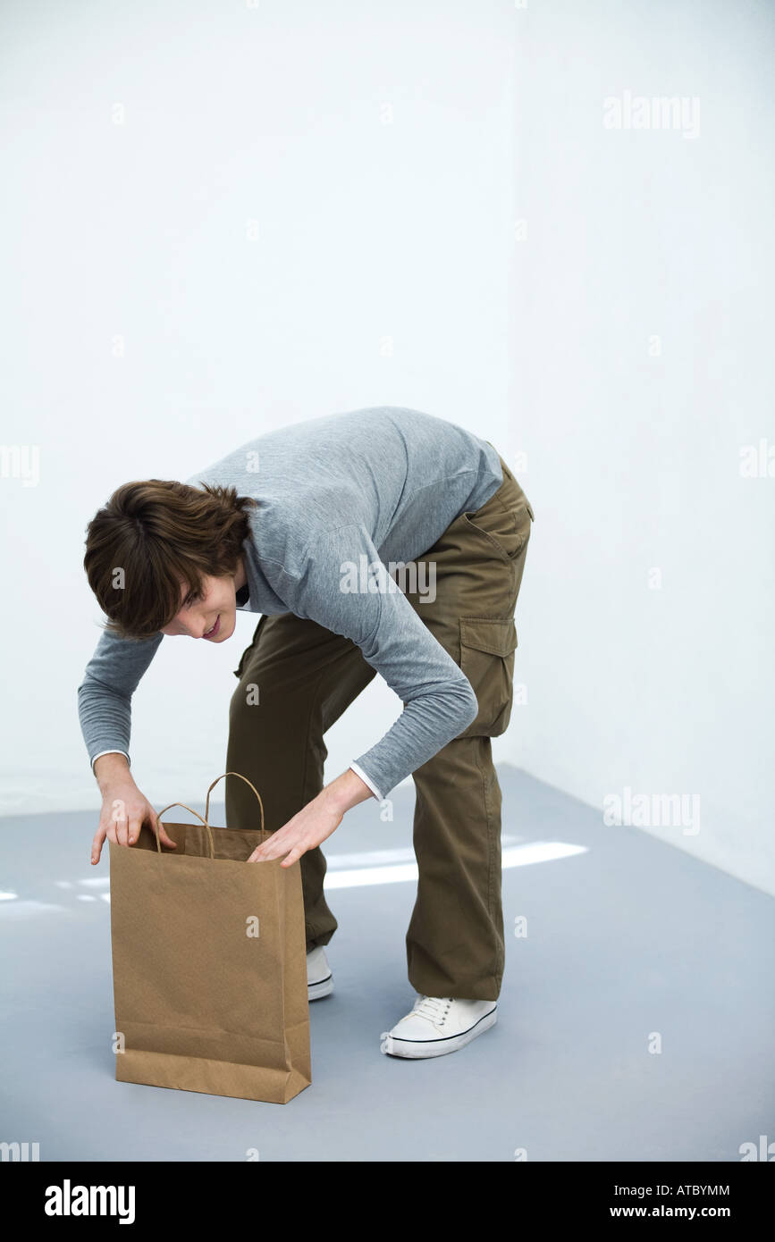 Young man bending over paper shopping bag, looking away, smiling Stock ...