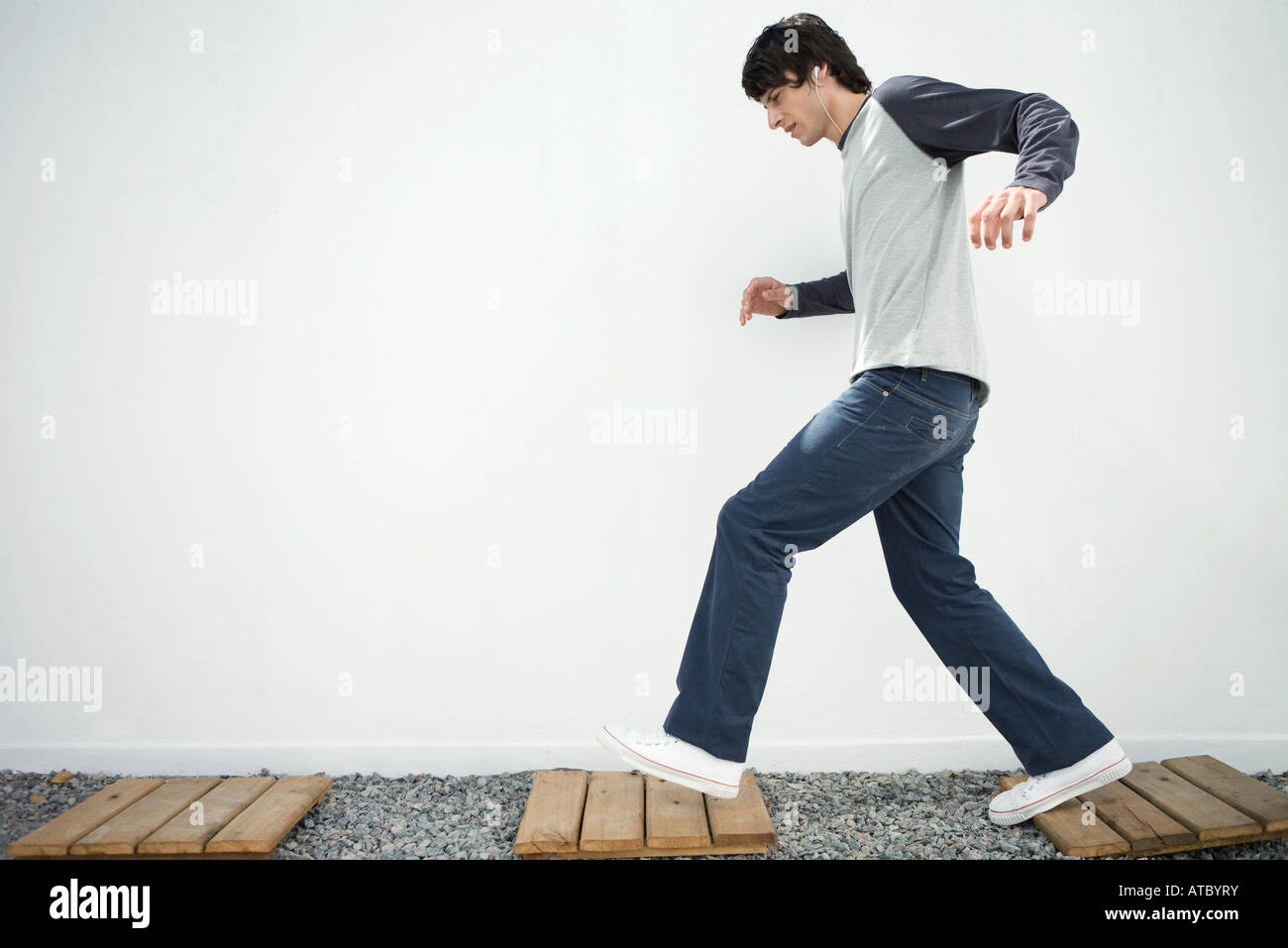 Young man walking on path, listening to earphones, side view Stock ...