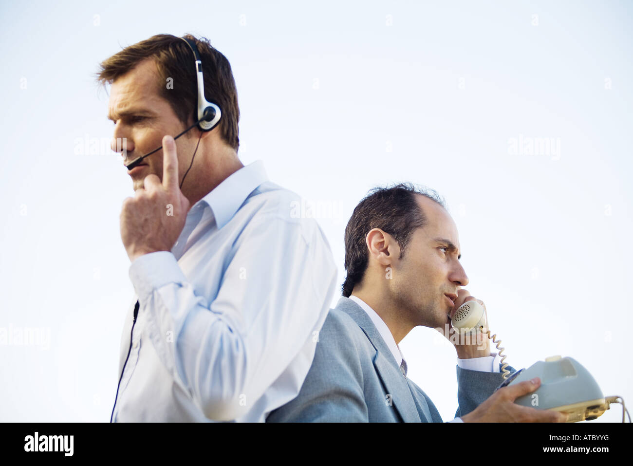 Two businessmen back to back, one using headset, the other using ...