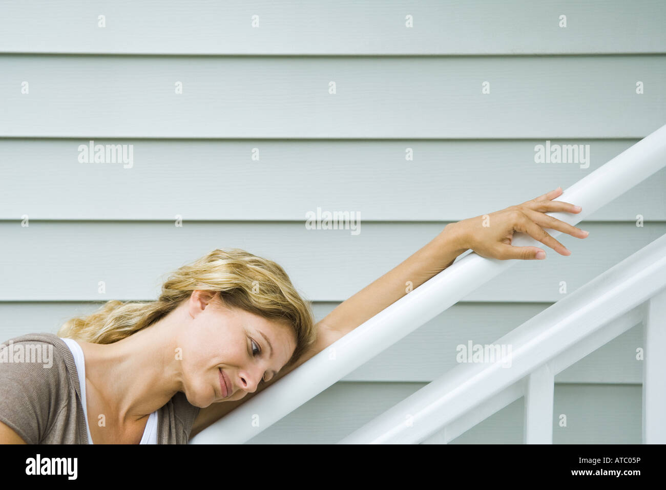 Woman leaning against railing, head resting on arm, smiling, side view ...