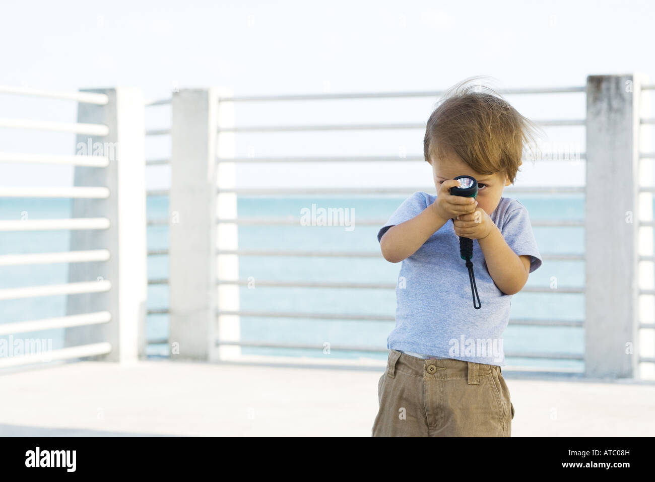 Toddler boy standing outdoors, hiding behind flashlight, peeking at ...