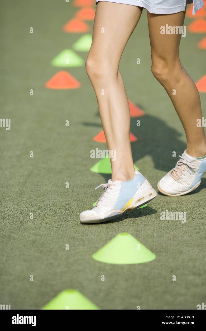 Teenage girl running through plastic cones, low angle view, cropped ...