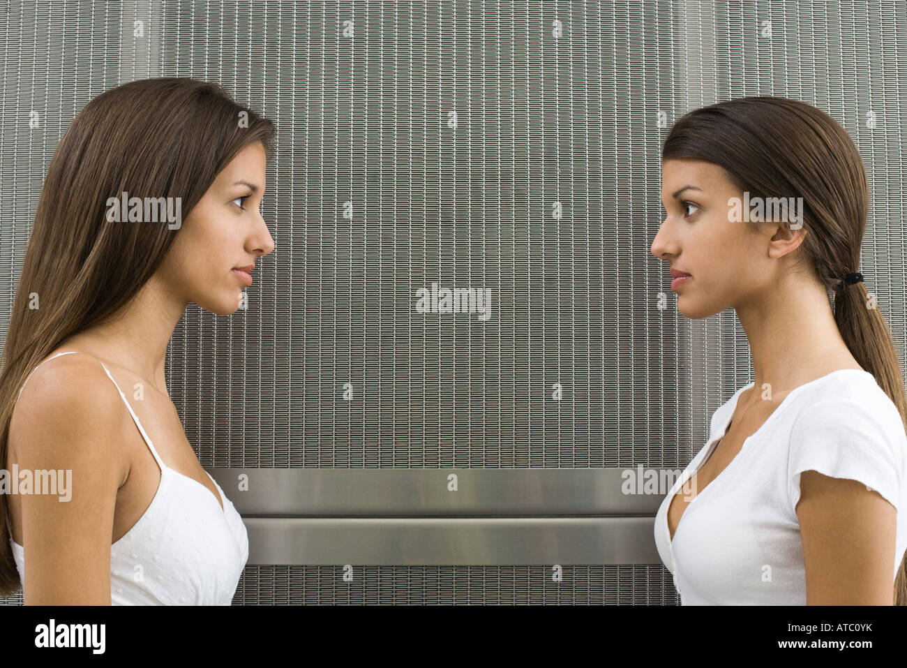 Teenage twin sisters face to face, looking at each other, side view ...