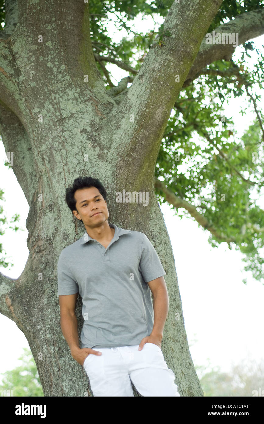 Man leaning against tree with hands in pockets, smiling Stock Photo - Alamy