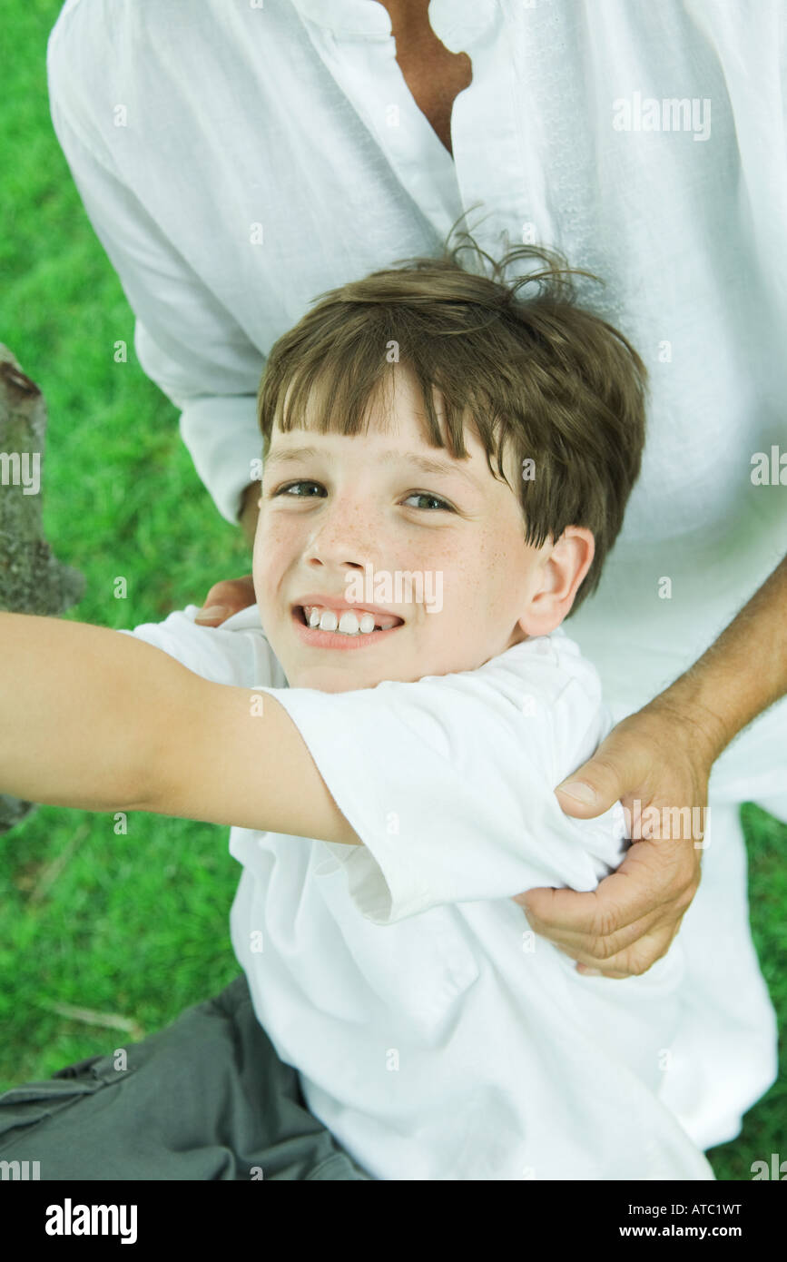 Boy with man's hands on his shoulders, smiling at camera, high angle ...