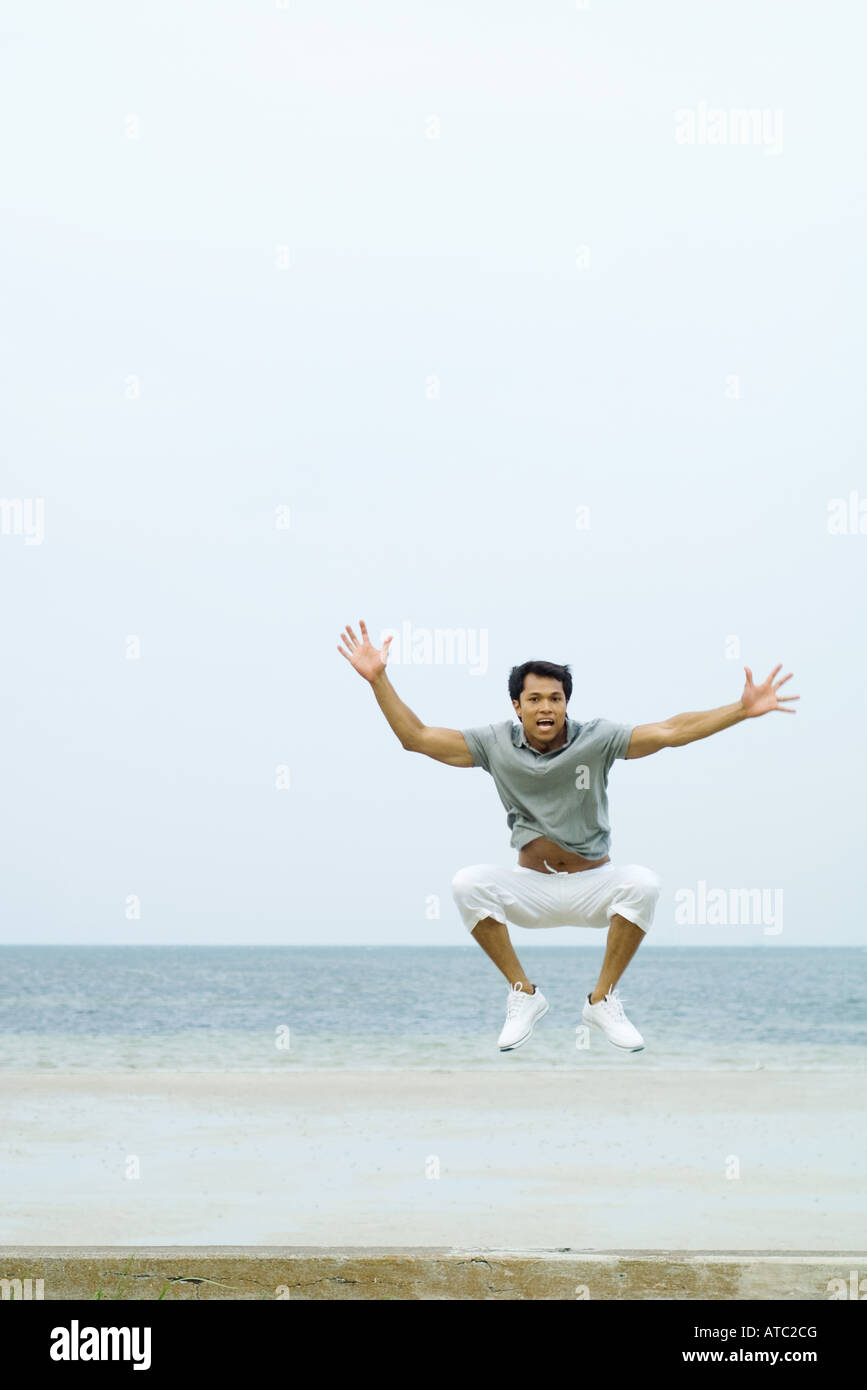 Man jumping in the air at the beach, arms out, looking at camera Stock ...