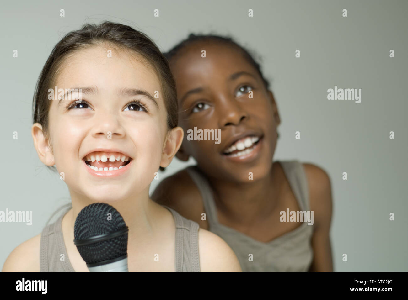 Two young girls singing into microphone together, both smiling and looking up Stock Photo - Alamy