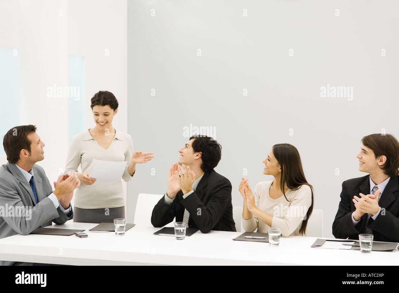 Businesswoman standing and speaking, seated colleagues clapping ...