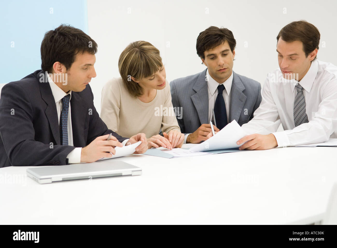 Four business partners sitting together at table, looking at document ...