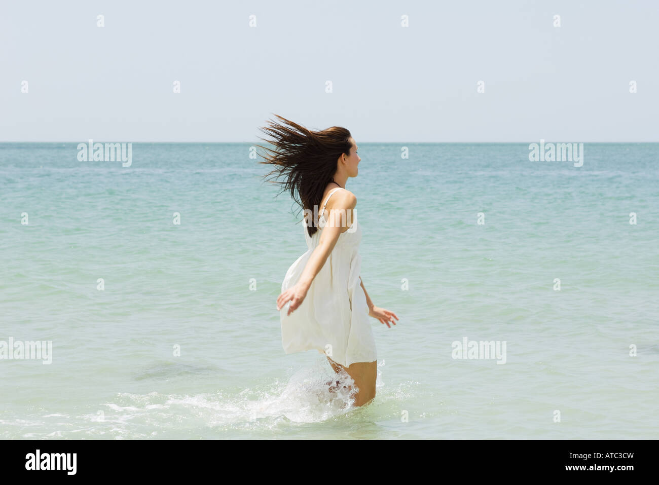 Young woman at the beach, running knee deep in water, rear view Stock ...
