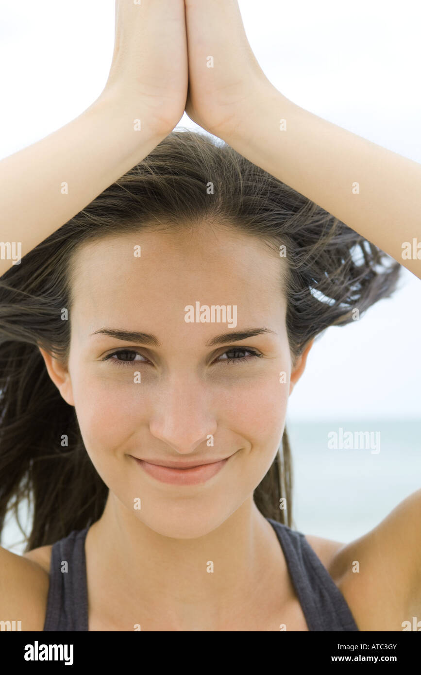 Young woman with hands raised over head in prayer position, smiling at ...