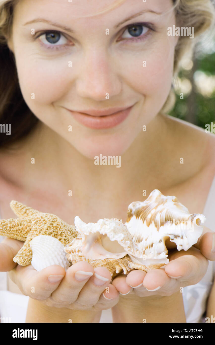 Woman holding up handfuls of seashells, smiling at camera Stock Photo ...