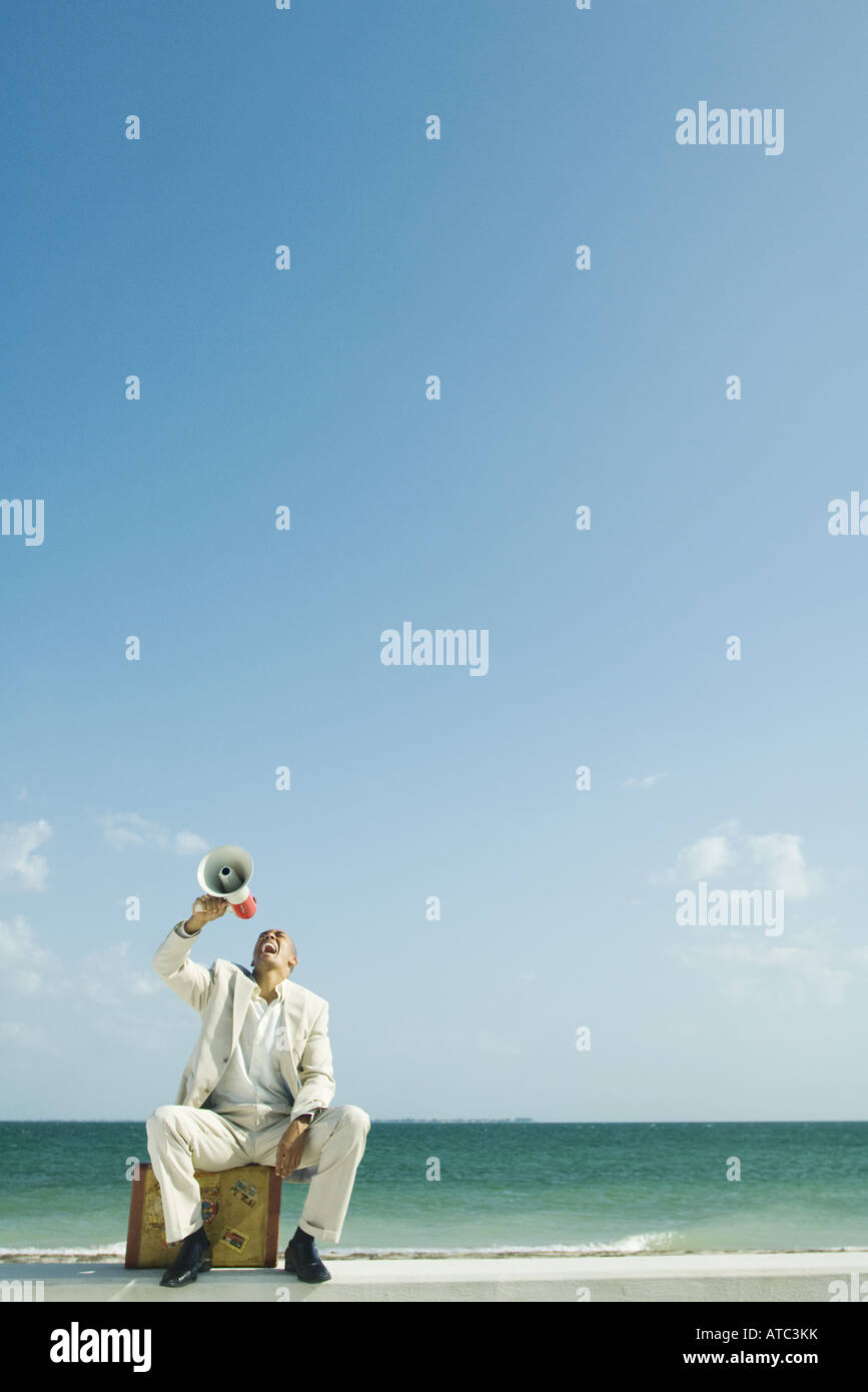 Man sitting on suitcase at the beach, shouting into megaphone Stock ...