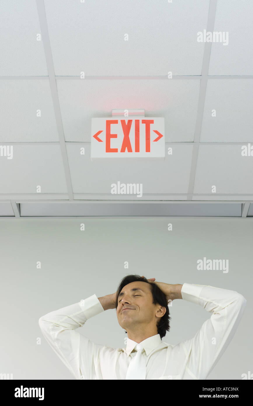 Man beneath "exit" sign with eyes closed, hands on head, smiling, low ...