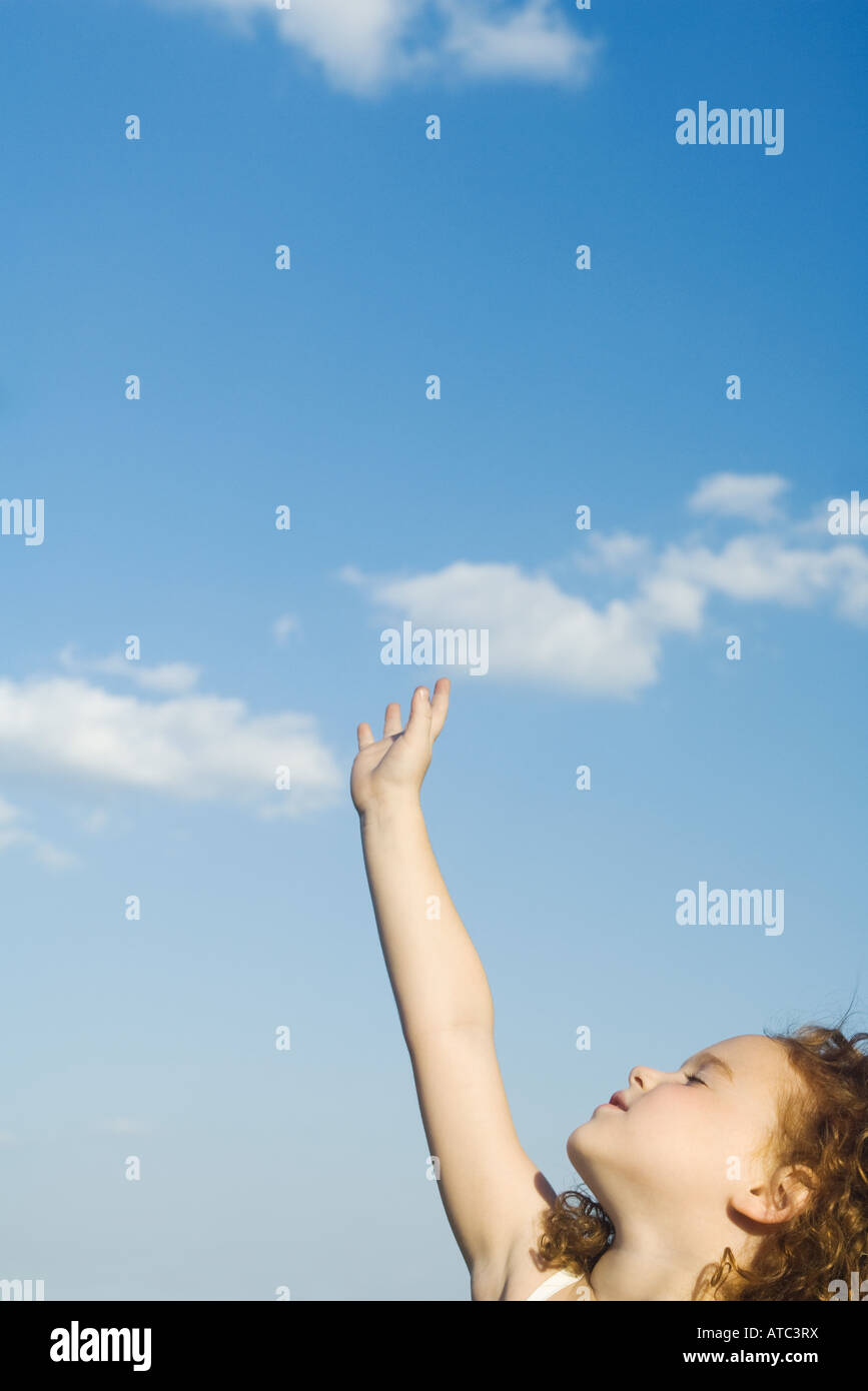 Little girl reaching one hand toward sky, head back, eyes closed ...